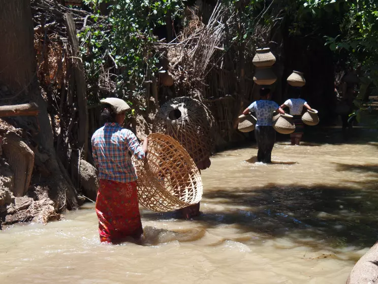 Drei Menschen mit Körben und Vasen waten in Myanmar durch knietiefe Fluten.